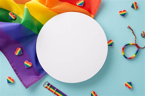 Lgbt 역사의 달을 위한 퍼레이드 필수품의 평평한 배치 무지개 깃발 핀 배지 화려한 하트 팔찌 파스텔 블루 표면에 문자나 메시지를 위한 빈 원이 있는 평면도 0명에 대한