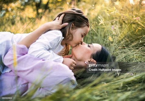 Happy Mother And Her Small Daughter Lying Down On The Grass In Spring Nature Kissing Foto De