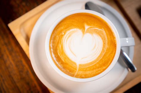 평면도 물 한 잔과 브라우니 한 조각과 함께 세라믹 화이트 컵 접시 및 숟가락에 담긴 라떼 아트를 곁들인 뜨거운 라떼 커피의 클로즈업 샷 0명에 대한 스톡 사진 및 기타