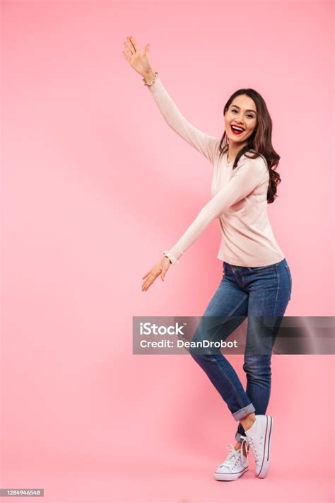 분홍색 배경에 고립 된 카피 스페이스의 큰 크기를 보여주는 청바지를 입고 긴 갈색 머리를 가진 예쁜 여성의 전체 길이 사진