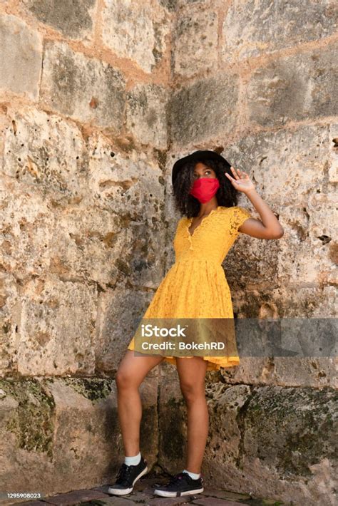 곱슬 머리를 가진 젊은 흑인 여성 빨간 마스크 노란색 드레스와 검은 모자를 입고 스타일과 태도 돌 벽 앞 20 24세에 대한 스톡 사진 및 기타 이미지 Istock