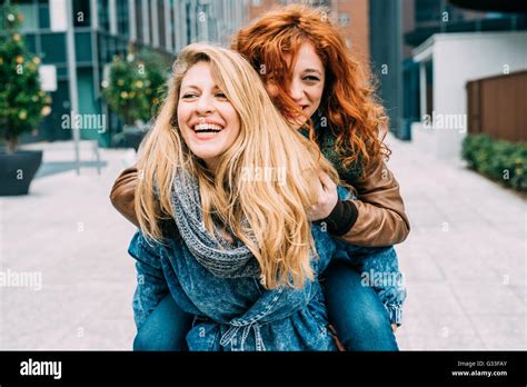 Half Length Of Two Blonde And Redhead Women Friemnds Having Fun Outdoor In The City Riding