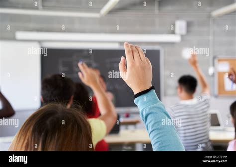 Rear View Of A Student In The Classroom Raising Her Hand To Ask A