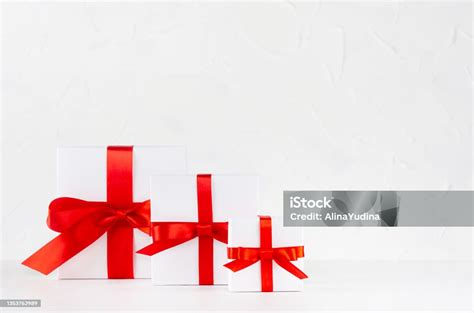 흰색 선물 상자는 빨간색 새틴 리본과 흰색 테이블에 활과 부드러운 빛 벽에 활 복사 공간을 다른 크기 3가지 개체에 대한 스톡