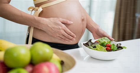 아시아 여성이 서서 믹스 슬래드 그릇을 들고 임신한 모습을 클로즈업합니다 매력적인 아름다운 젊은 여성 임신 스탠드와 자궁에서 아기를 만지고 부엌에서 건강 식품 또는 채식