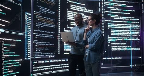 Portrait Of Two Diverse Developers Using Laptop Computer Discussing Lines Of Code That Appear
