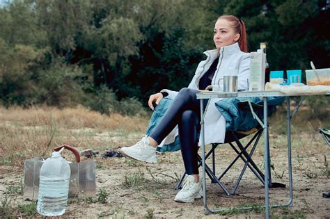 캠핑 아름다운 여성이 안락 의자의 관광 테이블에 앉아 소나무 숲에서 자연과의 단합을 즐기고 있습니다 40 44세에 대한 스톡 사진 및 기타 이미지 Istock