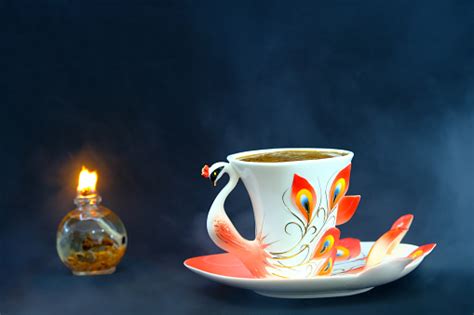 검은 색 배경과 테이블에 공작 모양의 커피 컵에 반짝이는 커피와 기름 램프를 굽기 그녀의 뒤에 서있다 0명에 대한 스톡 사진 및