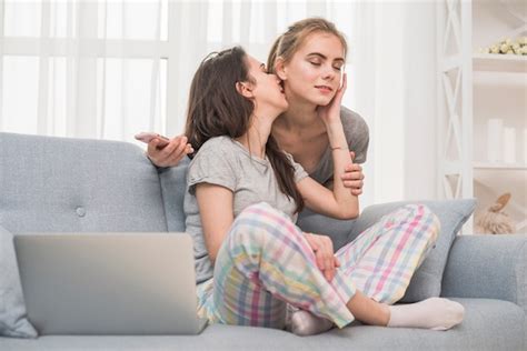 Jovem lésbica beijando a namorada segurando o celular na mão em casa Foto Grátis