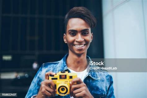 우르만 홍보 배경에 야외서 멋진 사진을 만들기 위해 손에 현대 노란색 카메라를 들고 아름다운 미소와 성공적인 숙련 된 사진