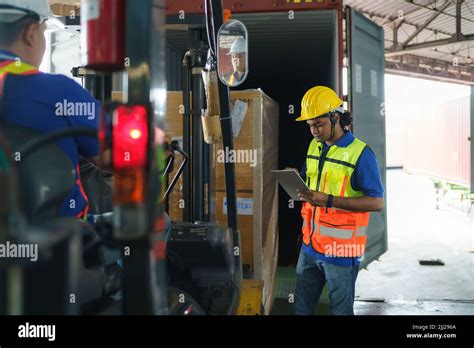 Asian Forklift Driver Loading A Shipping Cargo Container With A Full Pallet With Boxes In