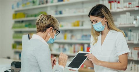 여성 약사가 보호 마스크를 착용하고 약국에서 고객에게 서비스를 제공하면서 디지털 태블릿을 보여줍니다 사진 Unsplash의