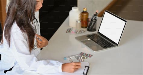 젊은 여성 약사가 의료 클립보드 알약 노트북 모형 및 책상 위의 비타민 병에 메모를 하고 처방전을 작성합니다 사진 Unsplash의 태국 이미지