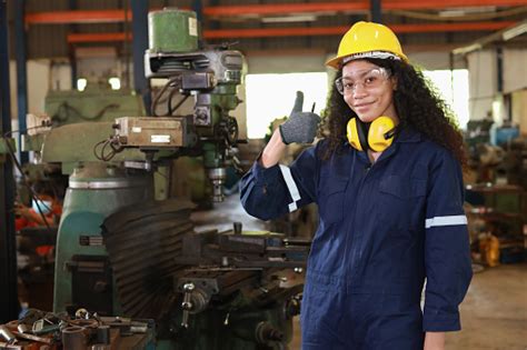 보호복을 입은 기술자 엔지니어 또는 노동자 여성이 미소를 지으며 엄지손가락을 치켜들거나 중공업 제조 공장에서 선반 금속 기계를 점검하고 있다 금속 가공 개념 16 17 살에