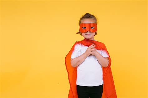 케이프와 빨간 마스크와 슈퍼 히어로로 옷을 입고 작은 금발 소녀 미소와 노란색 배경에 카메라를보고 4 5세에 대한 스톡 사진 및