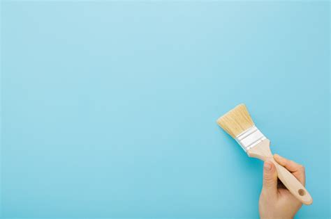젊은 성인 남자 손 들고 새로운 페인트 브러시 에 밝은 파란색 테이블 배경 파스텔 색상 근접 촬영 가정의 수리 작업을 위한 준비 텍스트의 빈 장소입니다 하향 보기 Diy에