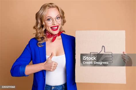 푸른 재킷과 빨간 스카프를 두른 쾌활한 여자가 베이지색 배경에 골판지 손 기호로 엄지 손가락 제스처를 표시합니다 30 34세에 대한 스톡 사진 및 기타 이미지 Istock