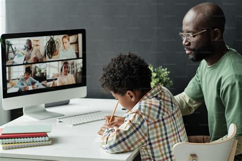 어린 소년은 선생님과 함께 책상에 앉아 글을 쓰고 온라인 대화 중에 컴퓨터로 공부하고 있습니다 사진 Unsplash의