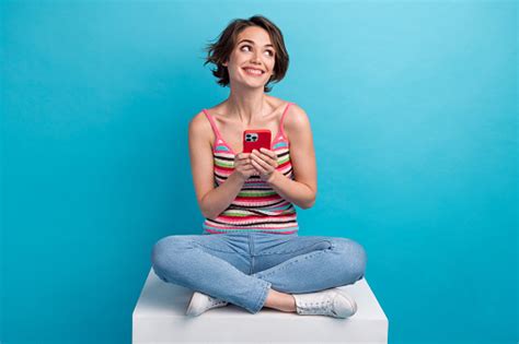 마음 속의 귀여운 사람의 전체 길이 초상화는 연단에 앉아 스마트폰을 들고 푸른 색 배경에 고립된 빈 공간을 본다 25 29세에