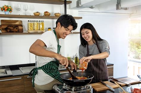 쾌활 한 행동에 앞치마 귀여운 행복 한 부부의 초상화 아침 식사 준비 현대 부엌에서 음식의 성분으로 장식 된 마 카로 니 테이블을 추가 하 고 좋은 시간을 보내고 2명에