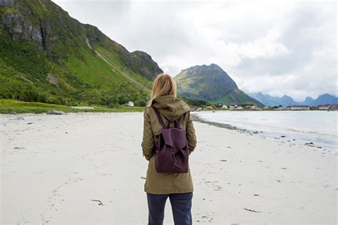 배낭을 가진 금발 머리 소녀는 빈 모래 바다 해변을 따라 산책 마을과 산 아름다운 자연 풍경입니다 외로운 소녀입니다 방황 여행 모험 라이프 스타일 노스 노르웨이 탐험 걷기에