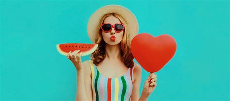 신선한 수박 조각과 여름 밀짚 모자 파란색 배경에 선글라스를 입고 그녀의 입술을 불고 큰 빨간 하트 모양풍선 아름다운 젊은