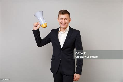 클래식 블랙 정장 스튜디오에서 회색 벽 배경에 고립 된 확성기를 들고 흰색 셔츠에 즐거운 젊은 비즈니스 남자의 초상화 업적 경력 자산 사업 개념 복사 공간을 모의 합니다