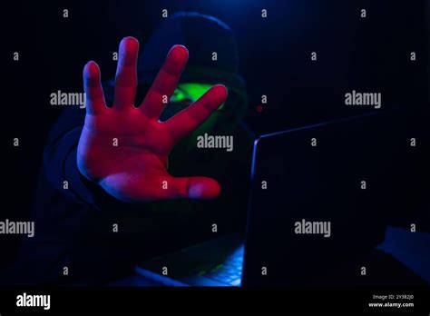 Cyber Hacker In Hood Behind Laptop Puts Hand Forward Hiding His Face In
