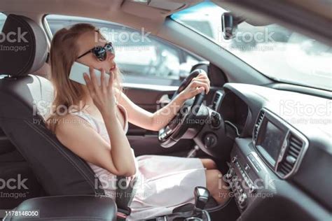 휴대 전화에 자동차의 내부 통화에 소녀 백미러에서 보이는 쇼핑 센터의 주차장에서 공원 스티어링 휠에 의해 고정 보유 분홍색 드레스를 입고 도시에서 여름 선글라스에 여자