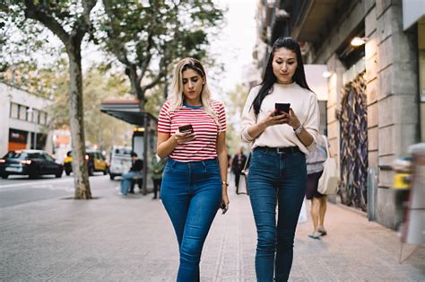 스마트 폰 가제트를 손에 들고 도시 환경에서 걷고 라이브 통신을 무시하는 두 명의 여성 네트워크에서 채팅하는 중독 된 힙스터 소녀 25 29세에 대한 스톡 사진 및 기타