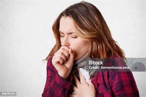 아름 다운 젊은 여성 모델의 스튜디오 샷 나쁜 기침 티슈를 사용 하 여 목에 스카프를 착용 느끼는 불쾌 하 고 건강에 해로운 흰색 콘크리트 배경 위에 절연 질병 및 질병