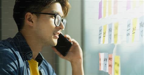 아시아 성인 자연 젊은 스마트 안경 캐주얼 천 집에서 작업 손 잡고 스마트 폰 Disscusion 원격 회의 다른 손으로 스티커 종이에 짧은 메모를 적어 창 유리에 메모