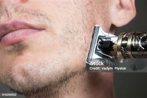 남자는 전기 금속 면도기 또는 건식 면도기로 수염을 자르고 있습니다 절단을위한 트리머 남자 얼굴에 짧고 희소 한 수염 모발 성장 문제 면도하지 않은 강모가 수염에 닿습니다