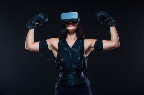 Ems 정장과 고립된 검은 색 배경에 권투 장갑을 가진 가상 현실 안경을 착용한 젊은 운동 여성 Ems 교육 전기 근육 자극기