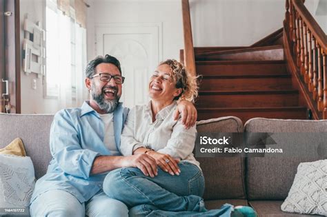 행복한 백인 커플이 거실 소파에 앉아 웃고 있다 남편과 아내는 집에서 소파에 앉아 큰 소리로 웃고 있습니다 현대 아파트에서 여가 시간을 보내는 남자와 여자 중년 커플에 대한
