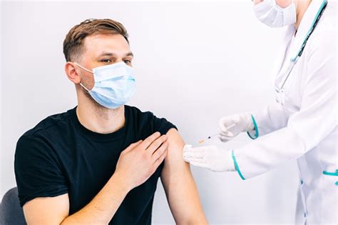 안전 마스크와 보호 장갑을 착용한 여성 간호사가 코로나19 팬데믹 기간 동안 의료 센터에서 남성 환자에게 백신 주사를 맞고 있다 바늘과 주사기를 사용하여 약을 주사하는 의사