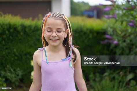 녹지와 꽃으로 둘러싸인 여름 뒤뜰에서 안경과 화려한 작은 머리띠가 있는 드레스를 입은 작고 귀엽고 웃는 긍정적인 소녀 건강한