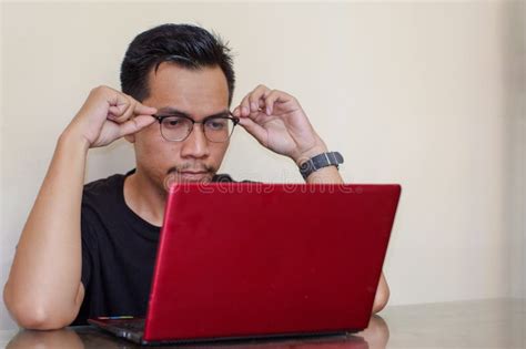 A Southeast Asian Serious Man Wearing Glasses Working On Laptop Online Sitting At Table