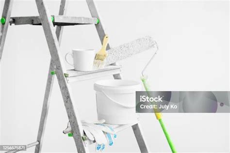 벽에 그림을 그리기 위한 도구 롤러 트레이 페인트 양동이 브러시 장갑 흰색 으로 칠해진 벽 근처의 사다리에 커피 한 잔 홈 리노베이션 기간 동안 커피 휴식 공간을 복사합니다