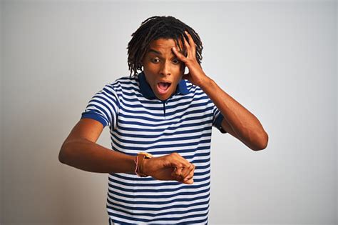 고립 된 흰색 배경 위에 서있는 줄무늬 파란색 폴로를 입은 공포를 가진 아프로 남자시계 시간을 보고 걱정 늦어질까 봐 두려워 걱정하는에 대한 스톡 사진 및 기타 이미지