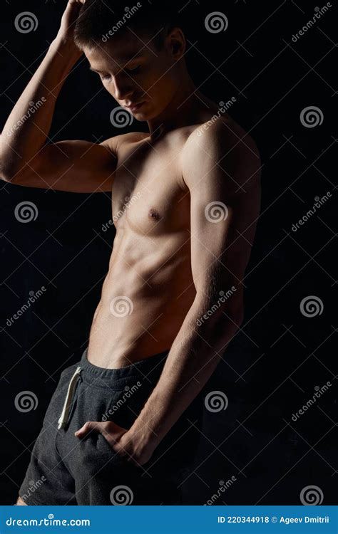 парень с голым торсом держит руку возле своего лица на черном фоне спортивный фитнес Стоковое