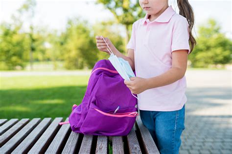 검역 후 학교의 첫 날 학교 근처에 머물고 배낭에서 보호 마스크를 꺼내는 어린 여학생 학생 코로나바이러스 전염병 중 학교에 다시