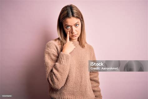 젊은 아름다운 금발의 여자 를 입고 겨울 울 스웨터 위에 분홍색 고립 된 배경 가리키는 눈을 보고 제스처 의심스러운 표정