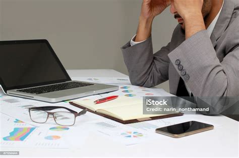 심각한 매력적인 젊은 잘생긴 사업가 전화 통화 및 현대 사무실에서 책상에 노트북 노트북 펜 문서 작업에 바쁜 사무실에서 책상에 앉아 그의 얼굴에 손을 유지 개미에 대한 스톡