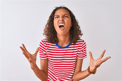 고립된 흰색 배경 위에 빨간색 줄무늬 티셔츠를 입은 젊은 브라질 여성이 공격적인 표정과 팔을 들고 미친 소리와 고함을 지르고 있습니다 좌절 개념입니다 T 셔츠에 대한 스톡