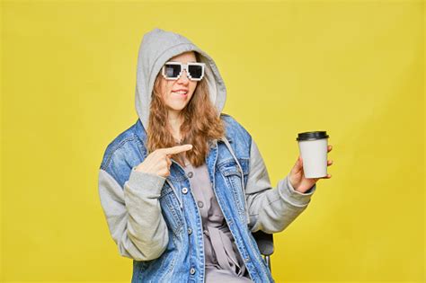 노란색 배경에 청바지와 안경 8 비트에 세련된 백인 소녀 일회용 커피 컵을 들고 가서 손가락을 가리킵니다 공간을 복사합니다 30 39세에 대한 스톡 사진 및 기타 이미지