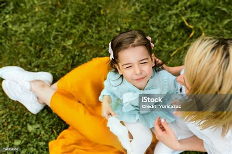 야외에서 함께 시간을 즐기고 그녀의 어머니와 함께 노는 행복 한 아이의 위에서 보기 그녀의 엄마와 함께 솜 사탕을 먹는 쾌활 한 어린 소녀 공원의 녹색 잔디에 앉아 어머니의