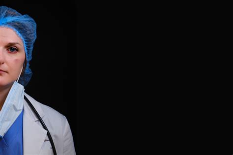 파란 의학 베레모에 마스크에서 상처와 상처를 가진 의사 텍스트 공간을 복사합니다 어두운 배경에 있는 간호사는 얼굴에 보호복의 흔적을 입고 클로즈업합니다 개념 코로나바이러스