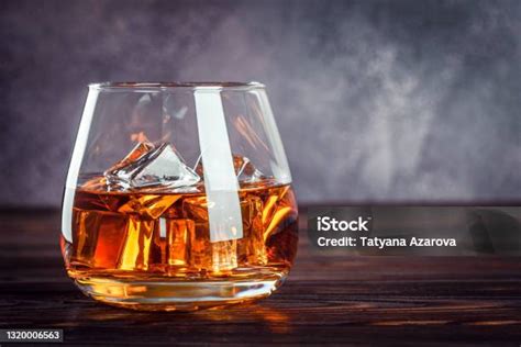 어두운 갈색 나무 테이블에 위스키 한 잔 얼음이 있는 투명한 노란색 알코올 음료 브랜디 버번 강한 알코올 음료 텍스트 템플릿을 위한 공간을 복사합니다 0명에 대한 스톡 사진