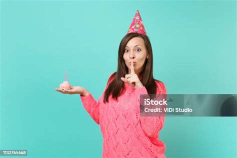 분홍색 스웨터 생일 모자에 예쁜 젊은 여자는 입술 쉿 제스처에 손가락으로 조용 하 고 파란색 배경에 고립 된 촛불 케이크를 개최 합니다 사람들 라이프 스타일 개념입니다 복사